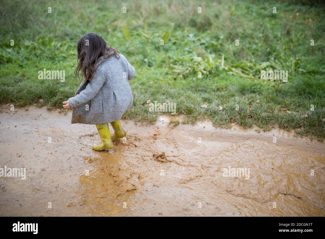 Happy little girl joyfully jumping and splashing in a muddy puddle ...