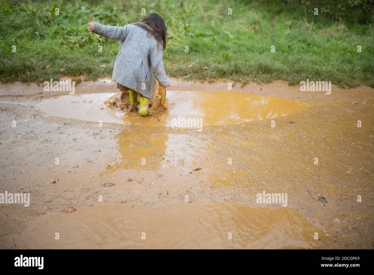 Happy little girl joyfully jumping and splashing in a muddy puddle ...