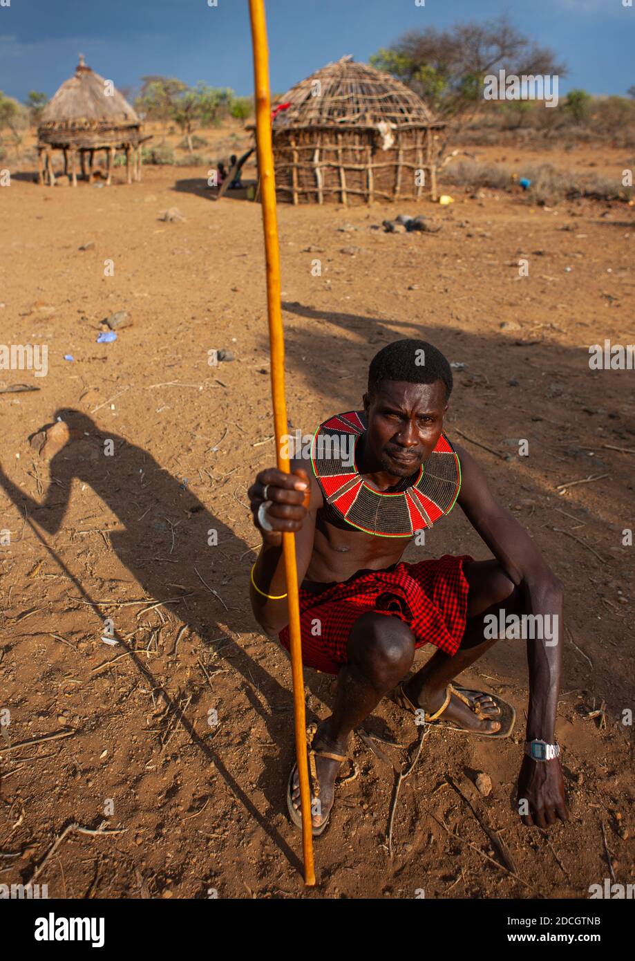 Portrait of a Pokot tribe man sit on his wooden pillow holding a spear ...