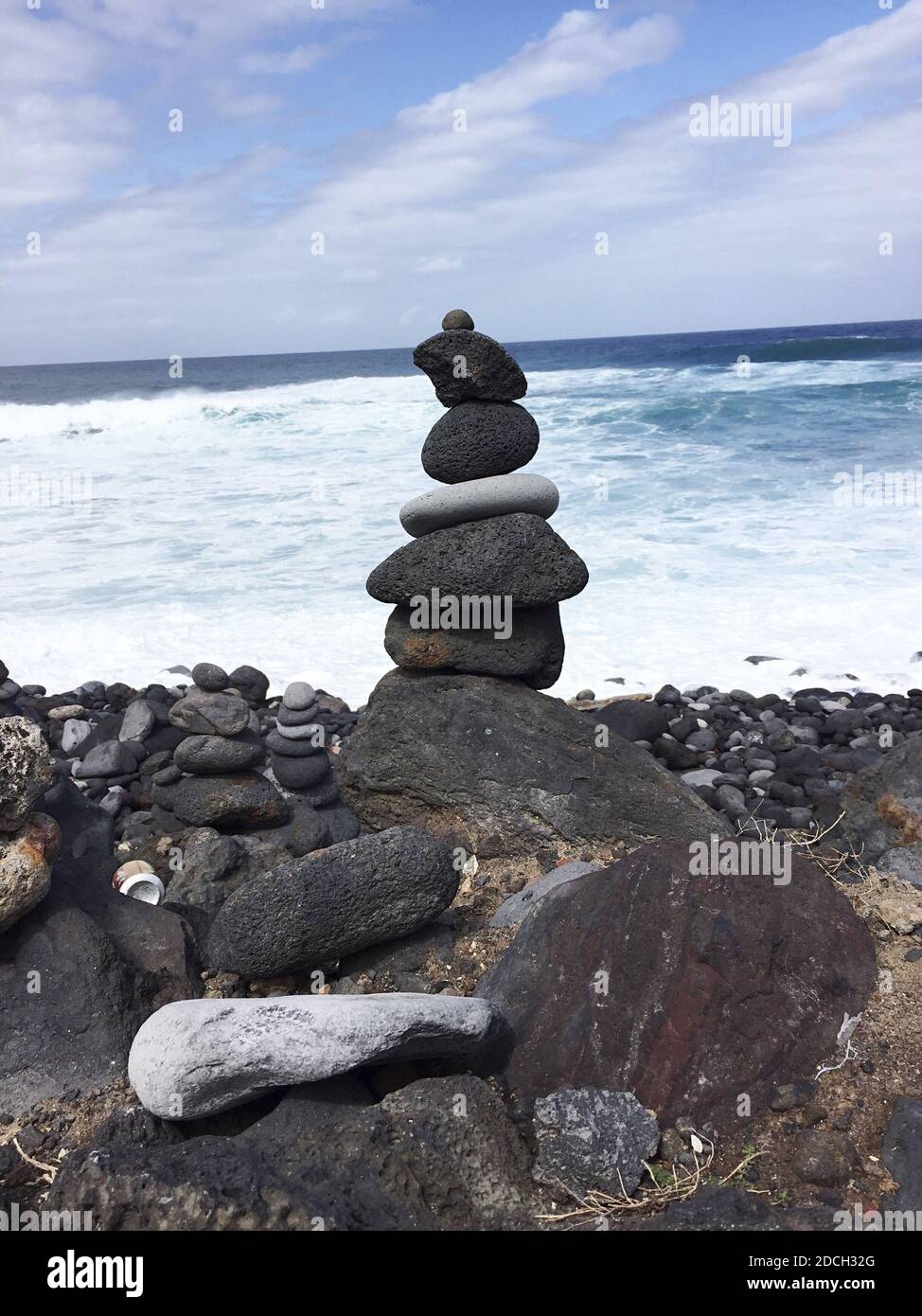A vertical shot of a pile of a balanced stone pyramid with a wavy sea ...