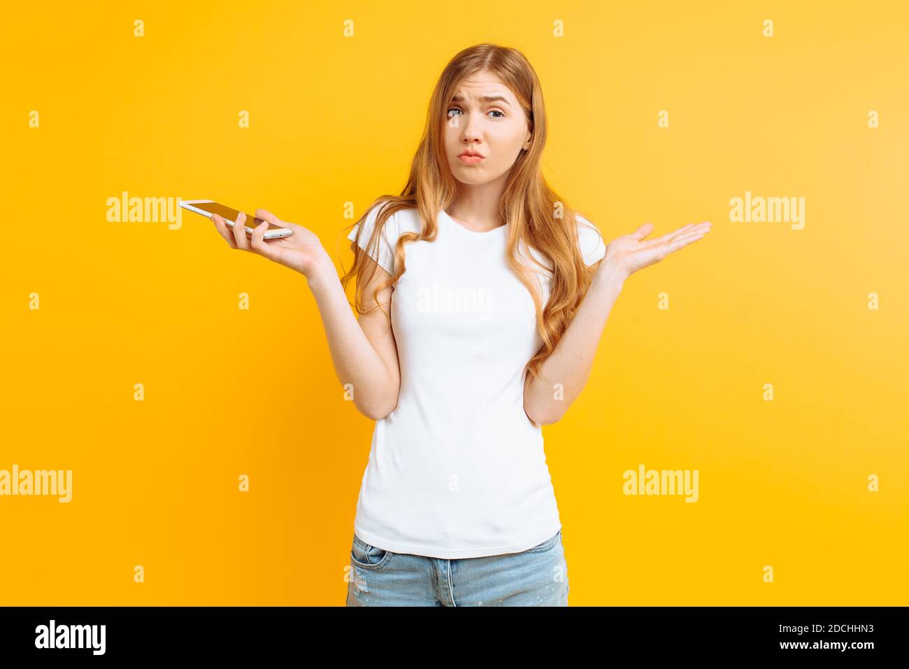 Uncertain woman with a phone in her hands, shrugs, with an indecisive ...