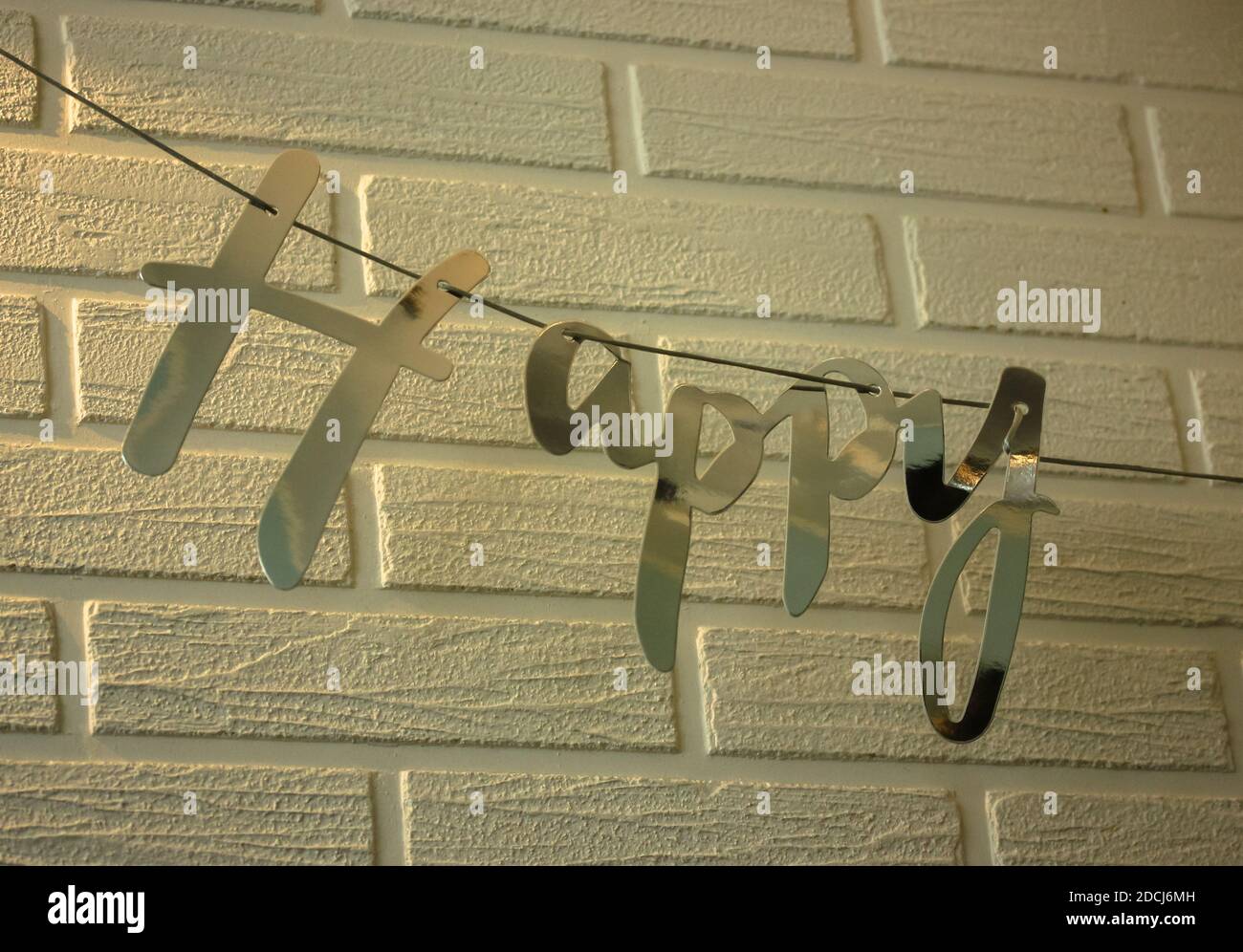 The word Happy is made of silver paper against a white brick wall ...