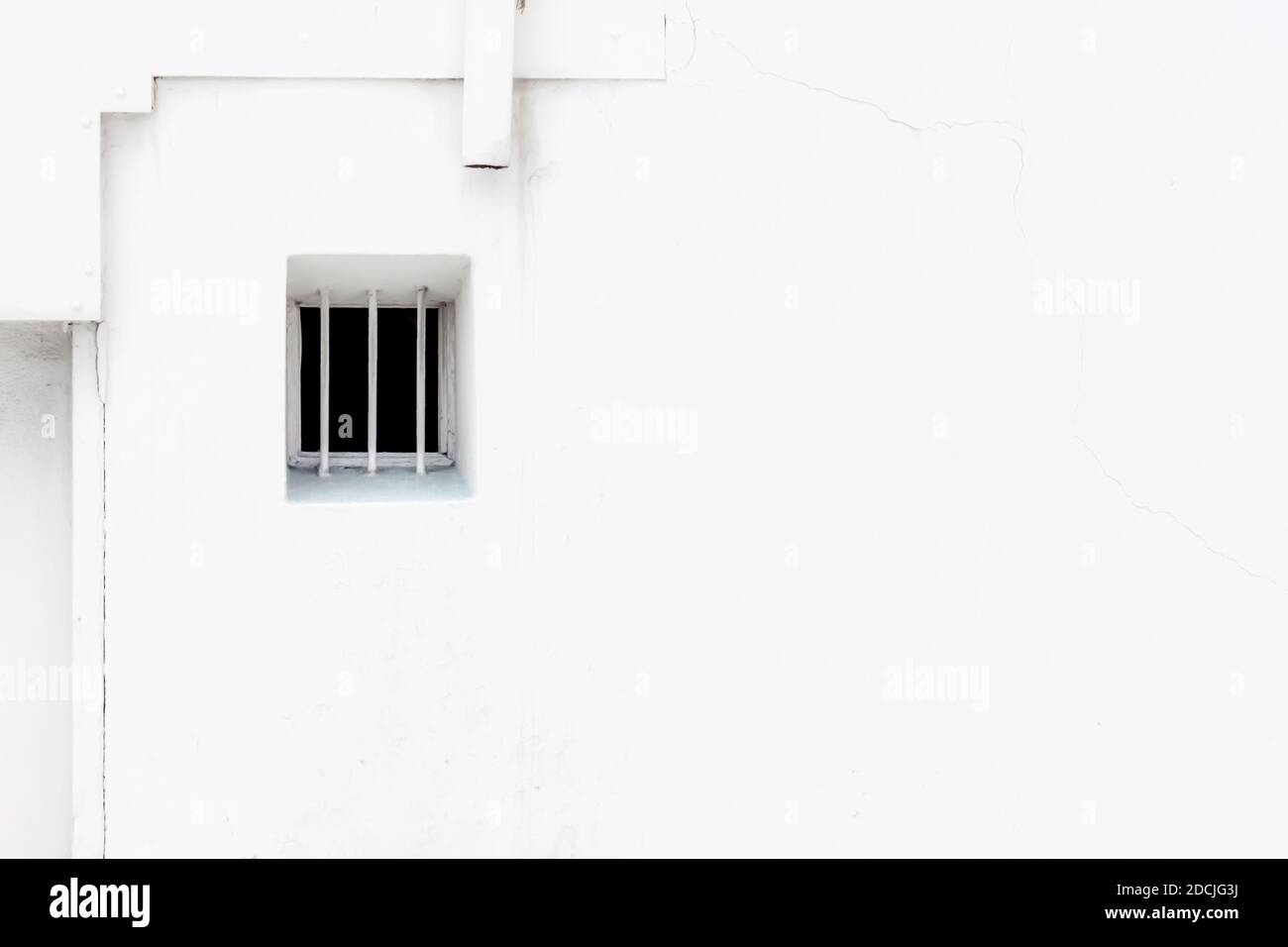 A closeup of a deep narrow prison window with bars on a white wall ...