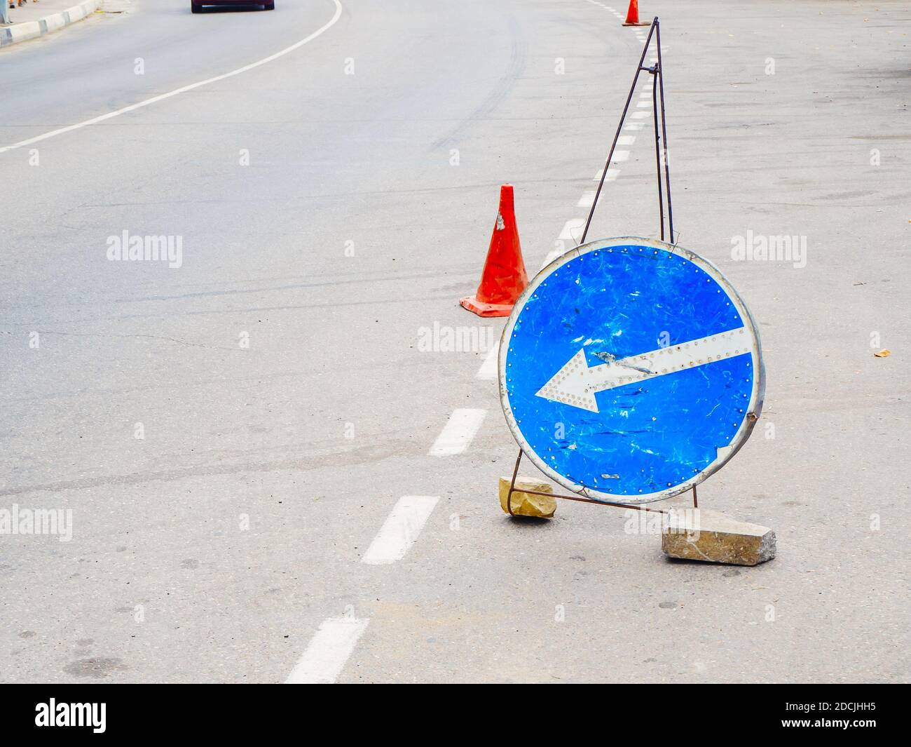Blue round sign with an arrow and a traffic cone stand on the asphalt ...
