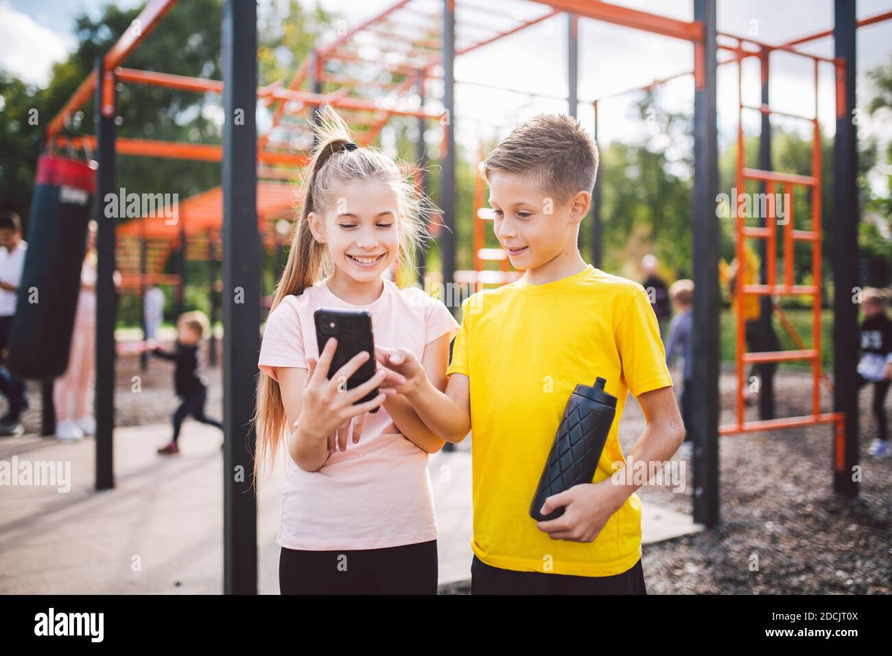Two children athletes use a smartphone at an outdoor gym. Twins boy and ...