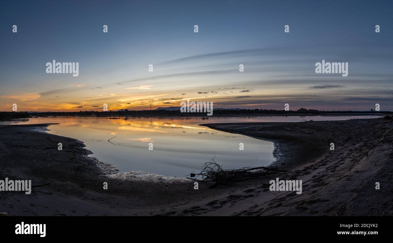 Estuary water surface reflects the golden sky with whispy clouds moving ...