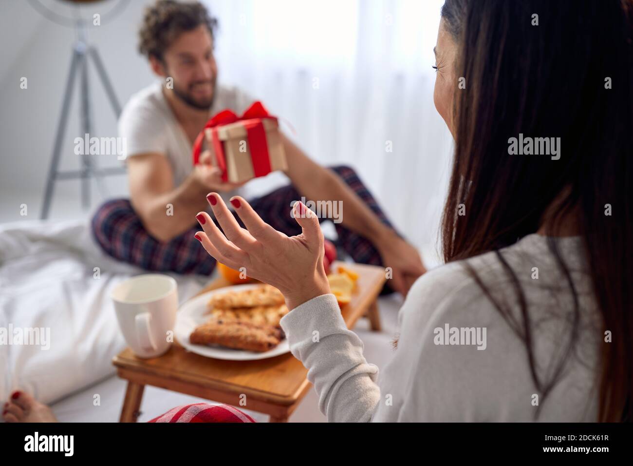 A Young Guy Giving A Xmas Present To His Excited Girlfriend Sitting In