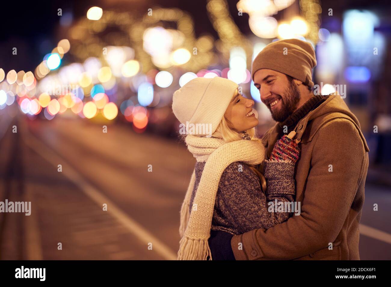 A young couple showing love while walking the city on a cold night ...