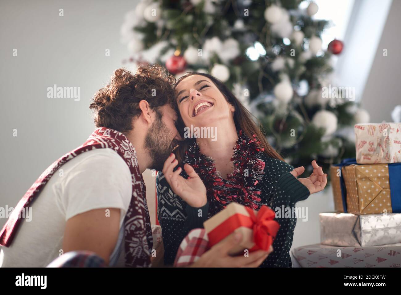 A young couple in moments of closeness at home giving Xmas presents on ...
