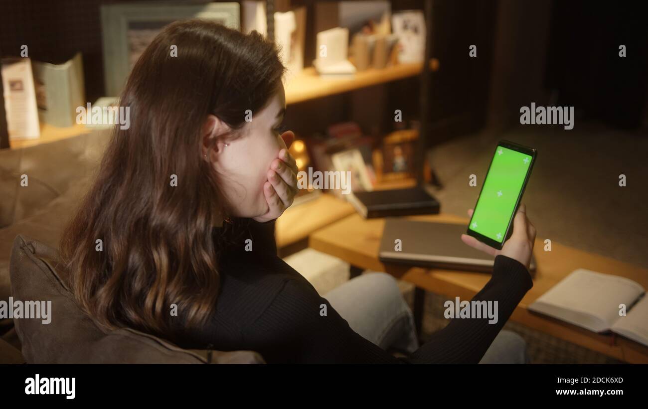 Beautiful woman with brown hair is sitting on the sofa at home, holding ...
