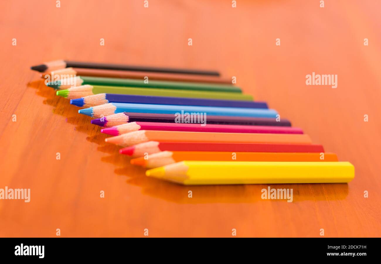 Diagonal perspective of twelve color pencils aligned on brown wood ...