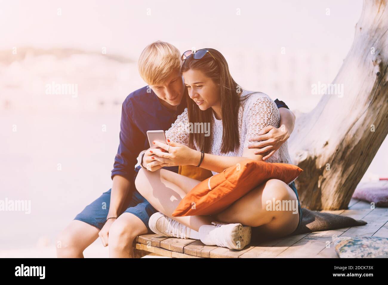 Young smiling white couple uses a smartphone on the beach in summer ...
