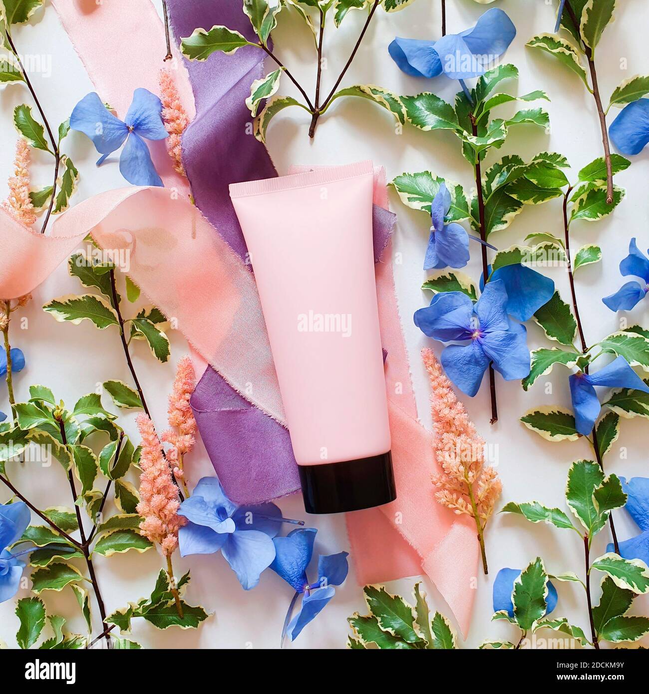 Mockup of pink squeeze bottle plastic tube with black cap, fresh greens ...