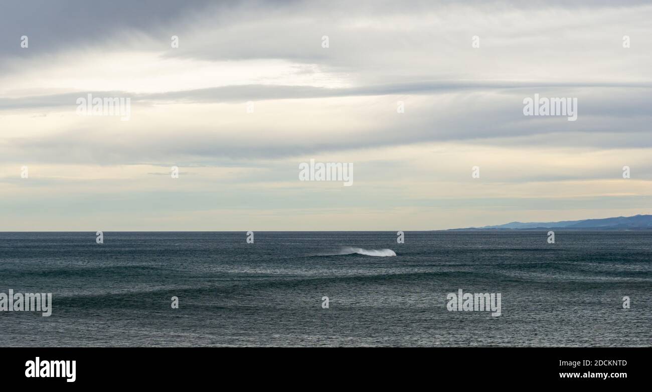 A large wave breaking in the ocean with copy space and blue and cloudy ...