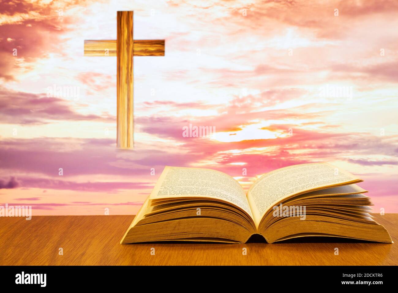 Open old bible on a wood table with blurred cross & colourful clouds ...