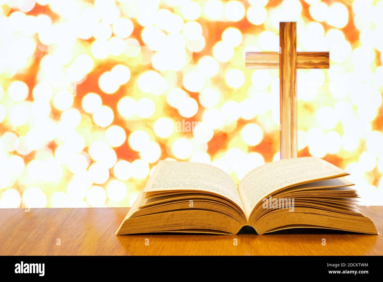 open old bible on a wood table with blurred cross & colourful sparking ...