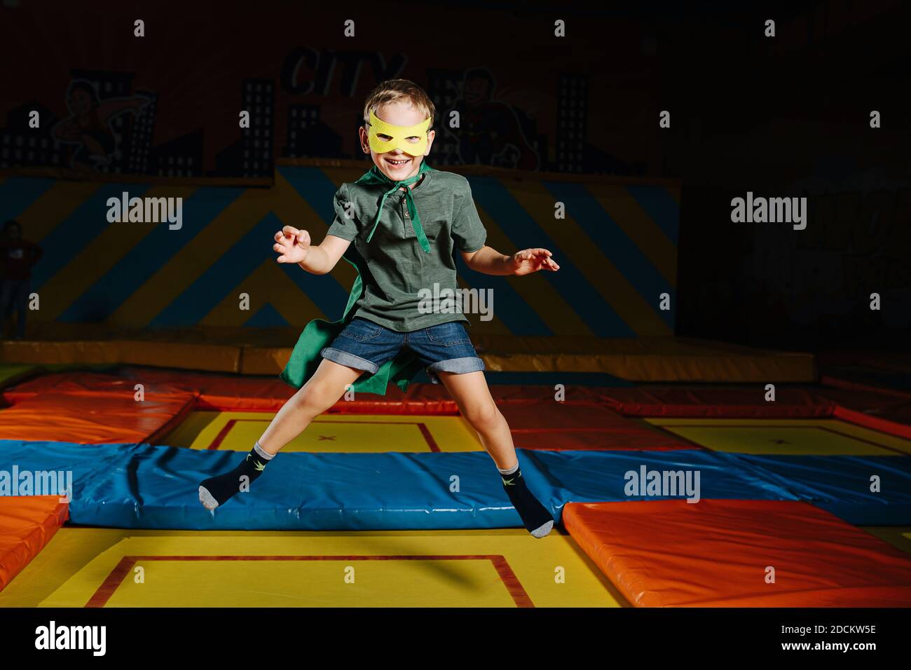 Mischievous confident boy in mask jumping on trampoline in ...