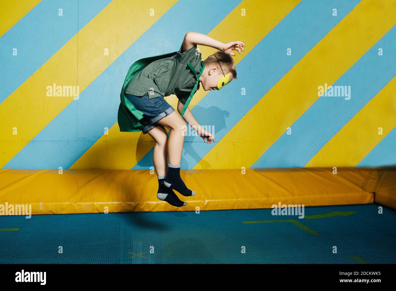 Boy in mask and cape jumping on trampoline in entertainment center ...