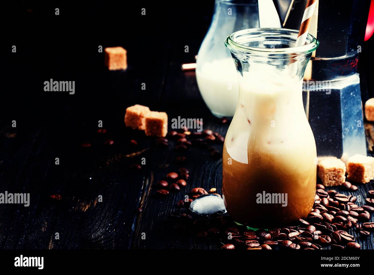 Cold iced coffee with milk and ice in a glass jug, dark background ...