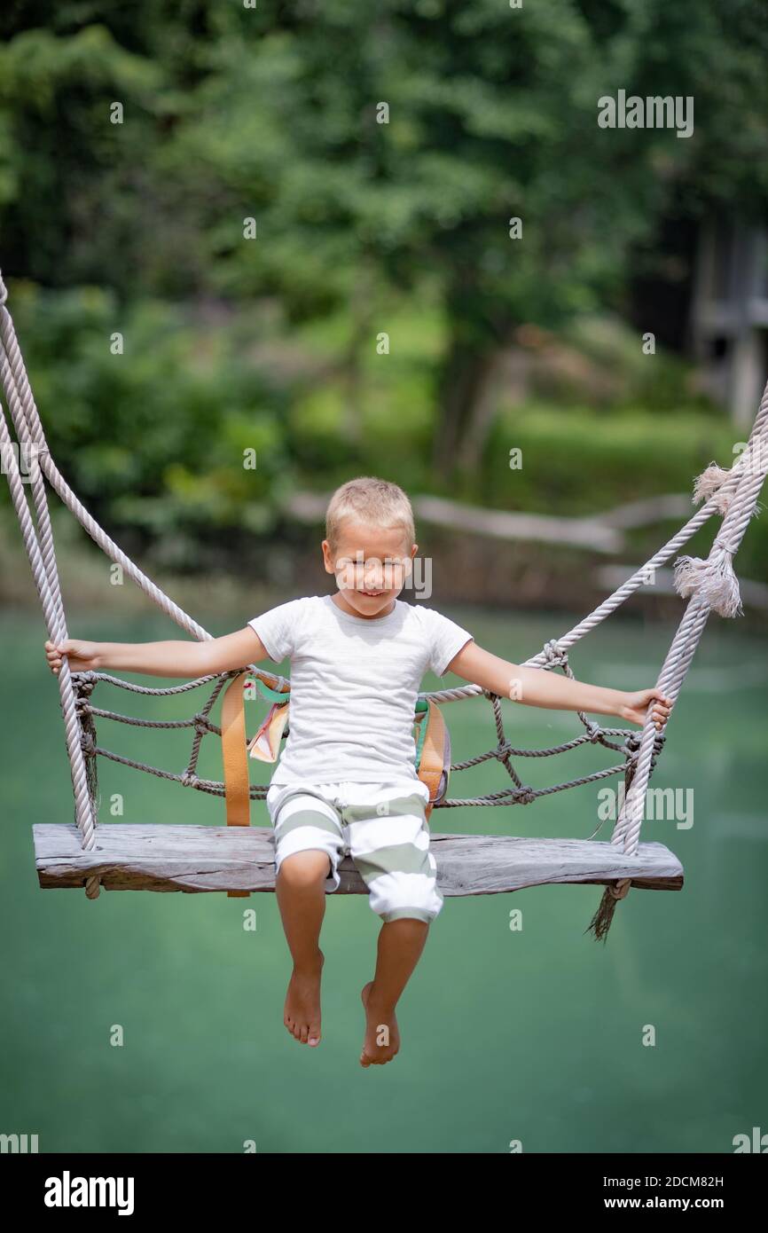 Little boy swinging on a swing over the river Stock Photo - Alamy