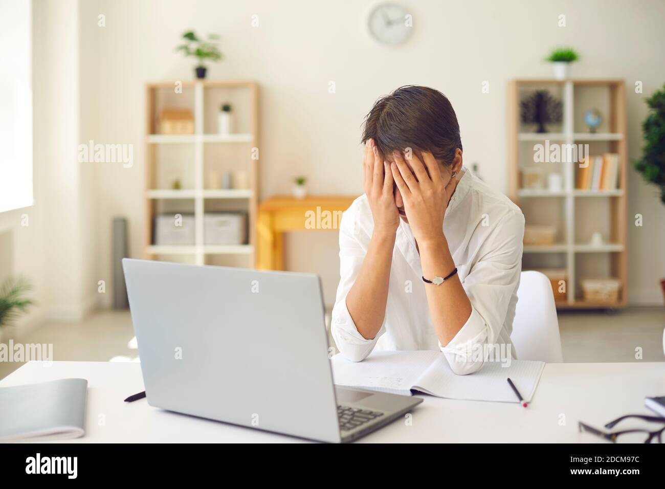 Overworked female manager closes face with tired hands sitting in front ...