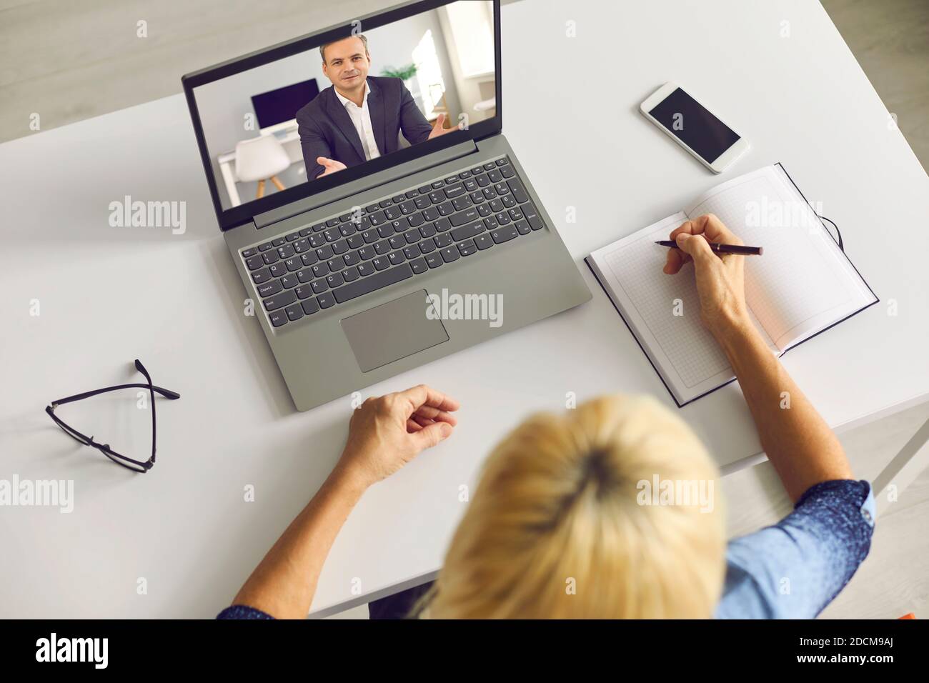 Senior woman taking notes while having video call with colleague or ...