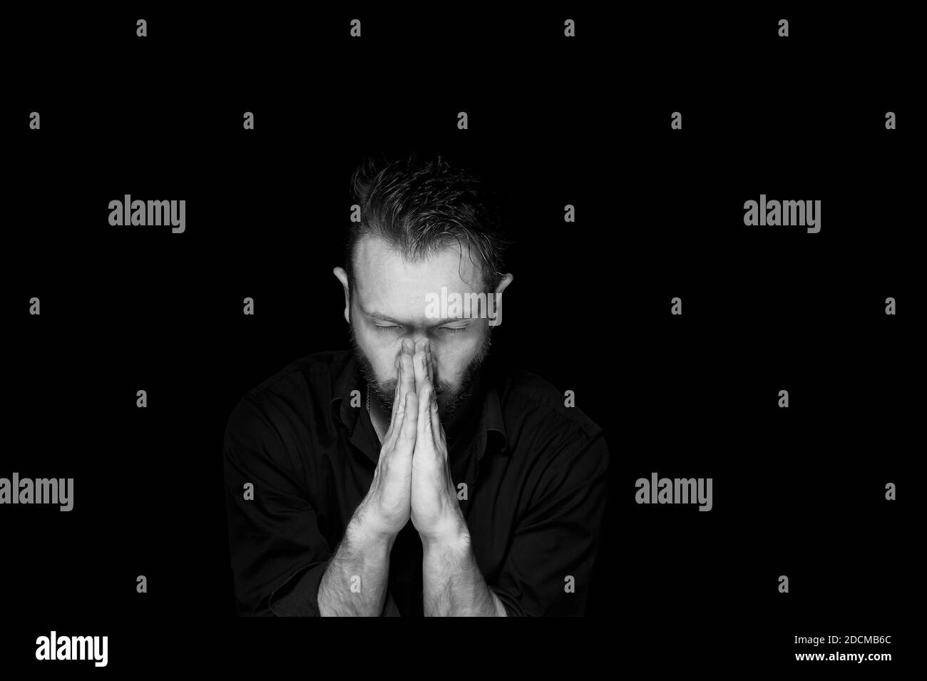 A man on a black background. Hands are folded in the position of prayer ...