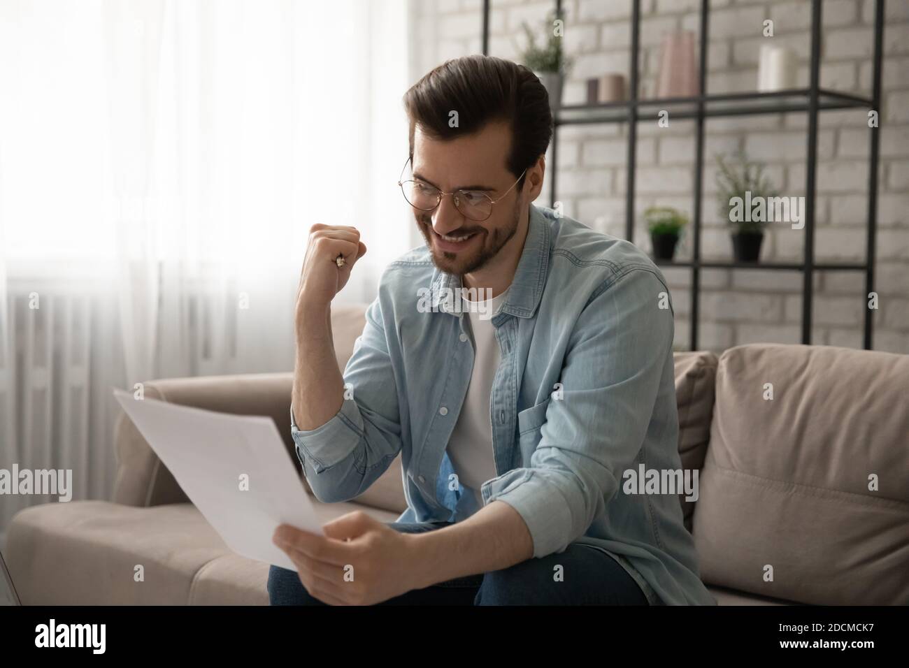 Emotional happy positive young man celebrating success, reading paper ...