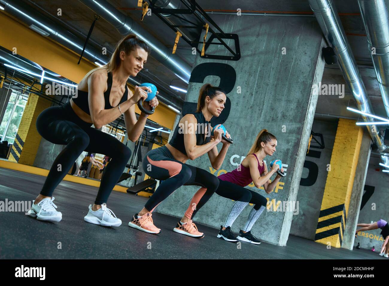 Full length of three young strong fitness girls exercising with iron ...