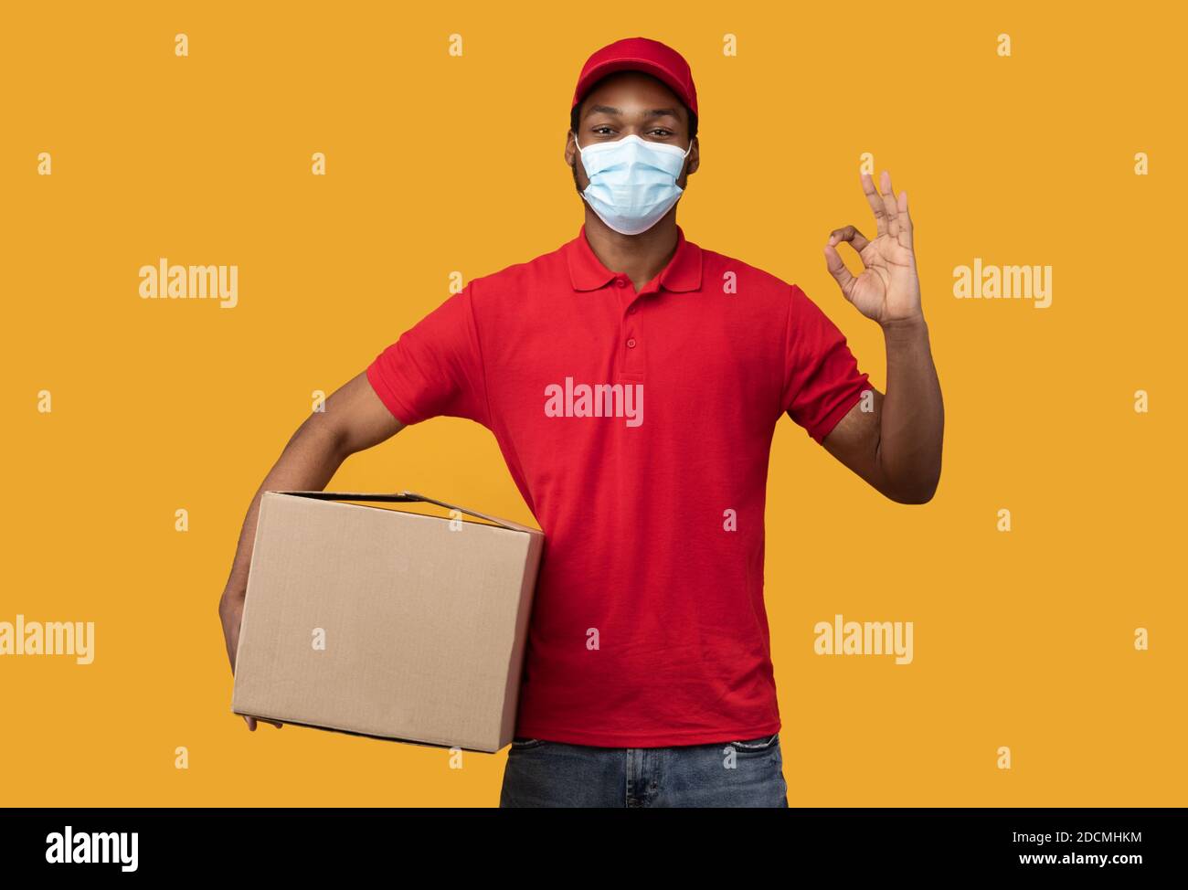 Black delivery man in mask holding box, showing okay gesture Stock ...