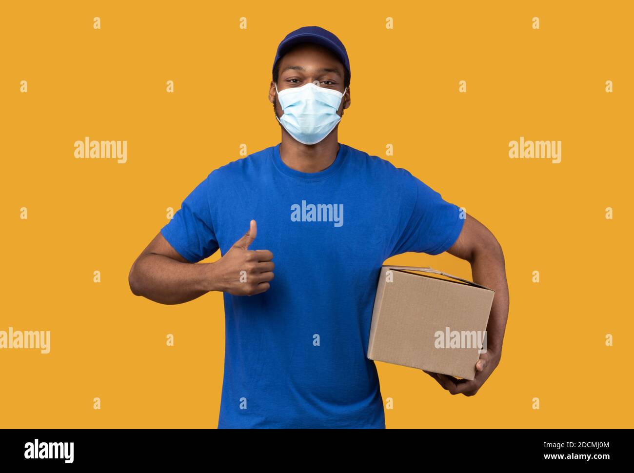 Black delivery man in mask holding box, showing thumbs up Stock Photo ...