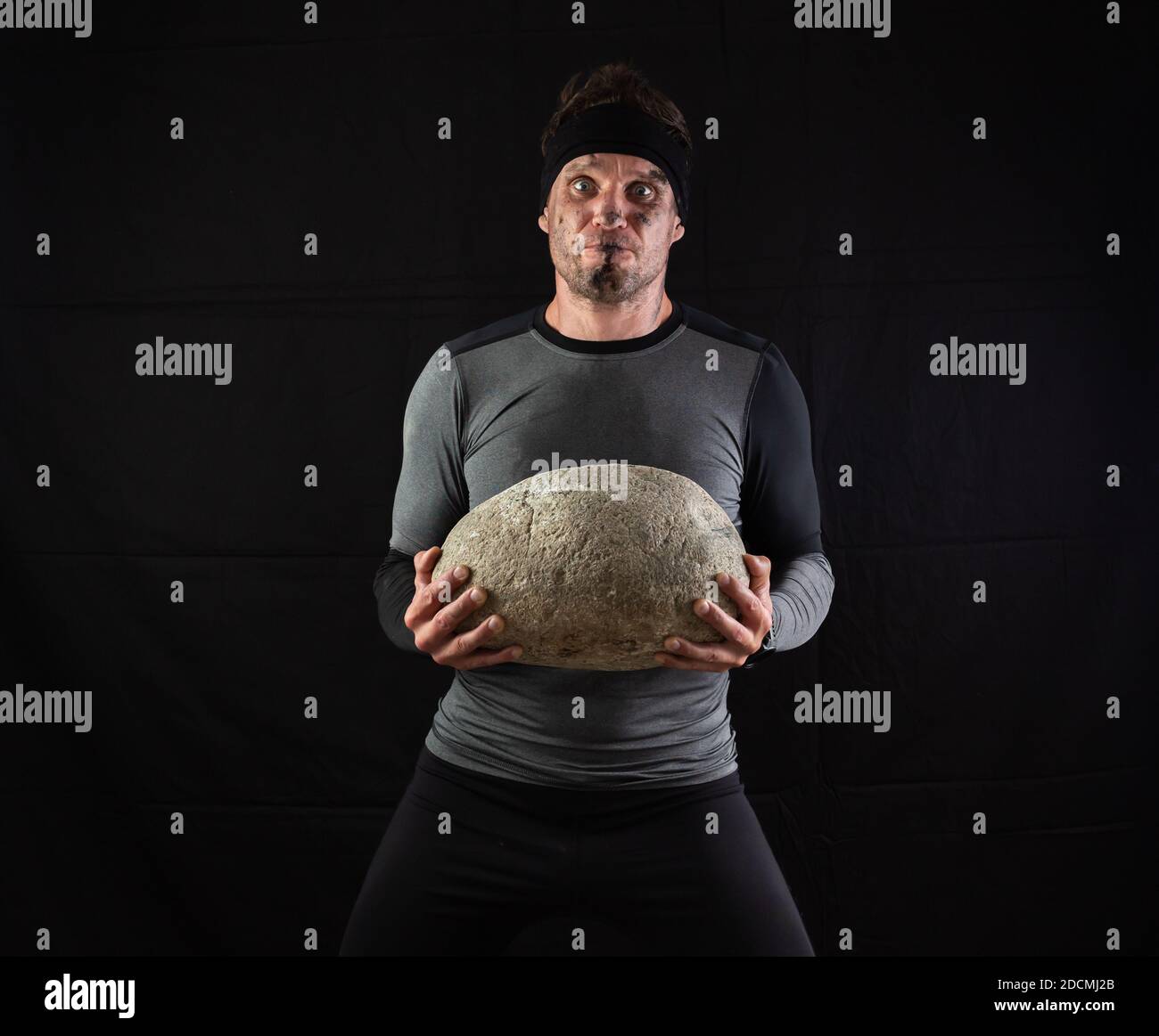 Sporty man holding a large heavy stone in his hands on a black ...