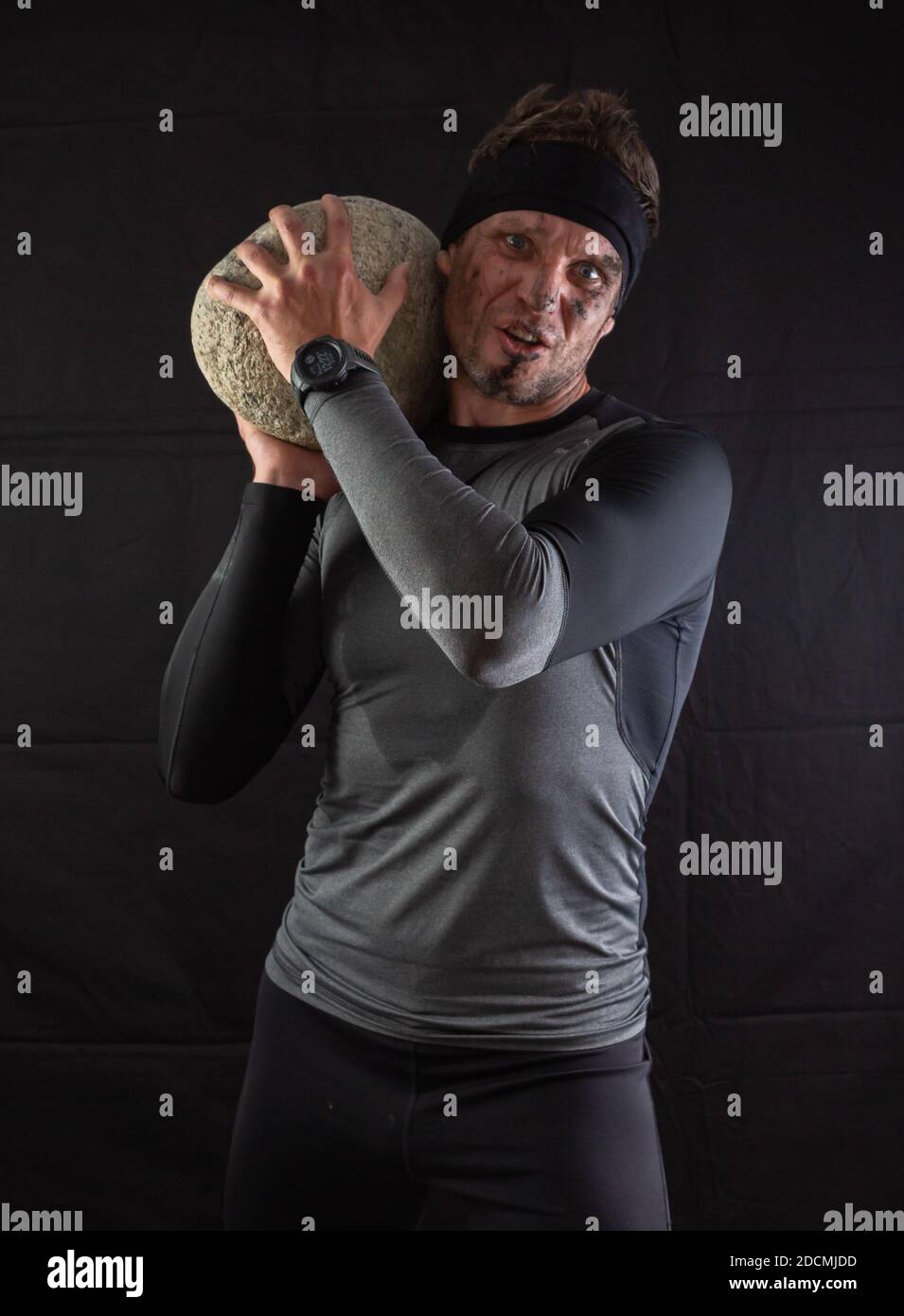 Sporty man holding a large heavy stone in his hands on a black ...