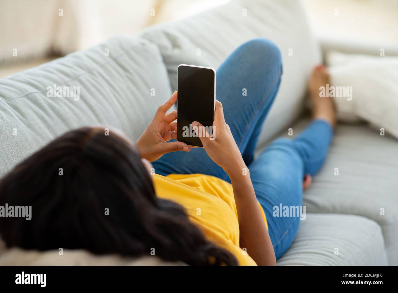 Unrecognizable black woman using cellphone on comfy sofa at home ...