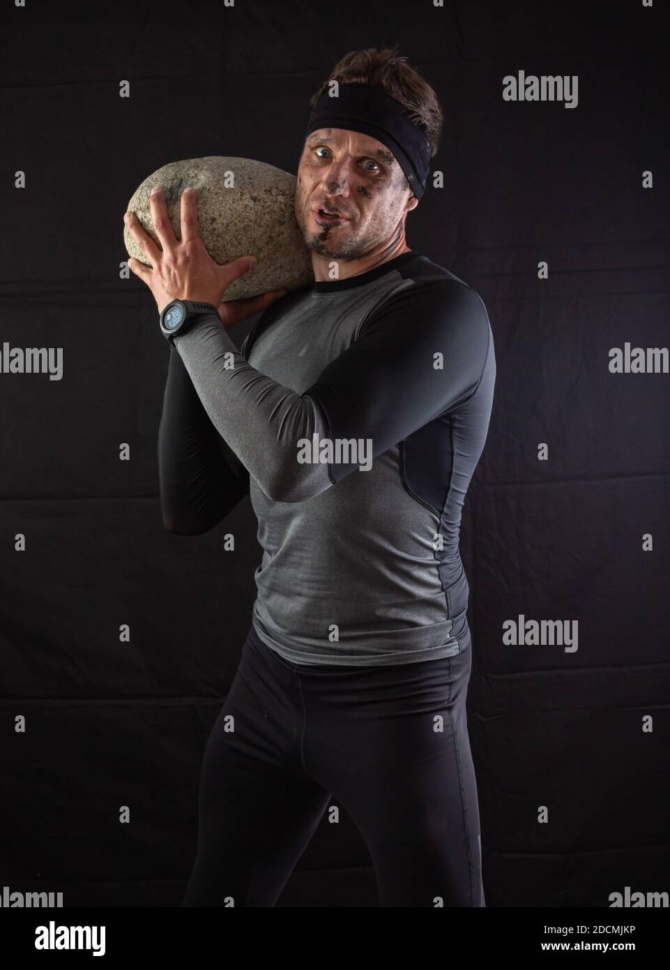 Sporty man holding a large heavy stone in his hands on a black ...