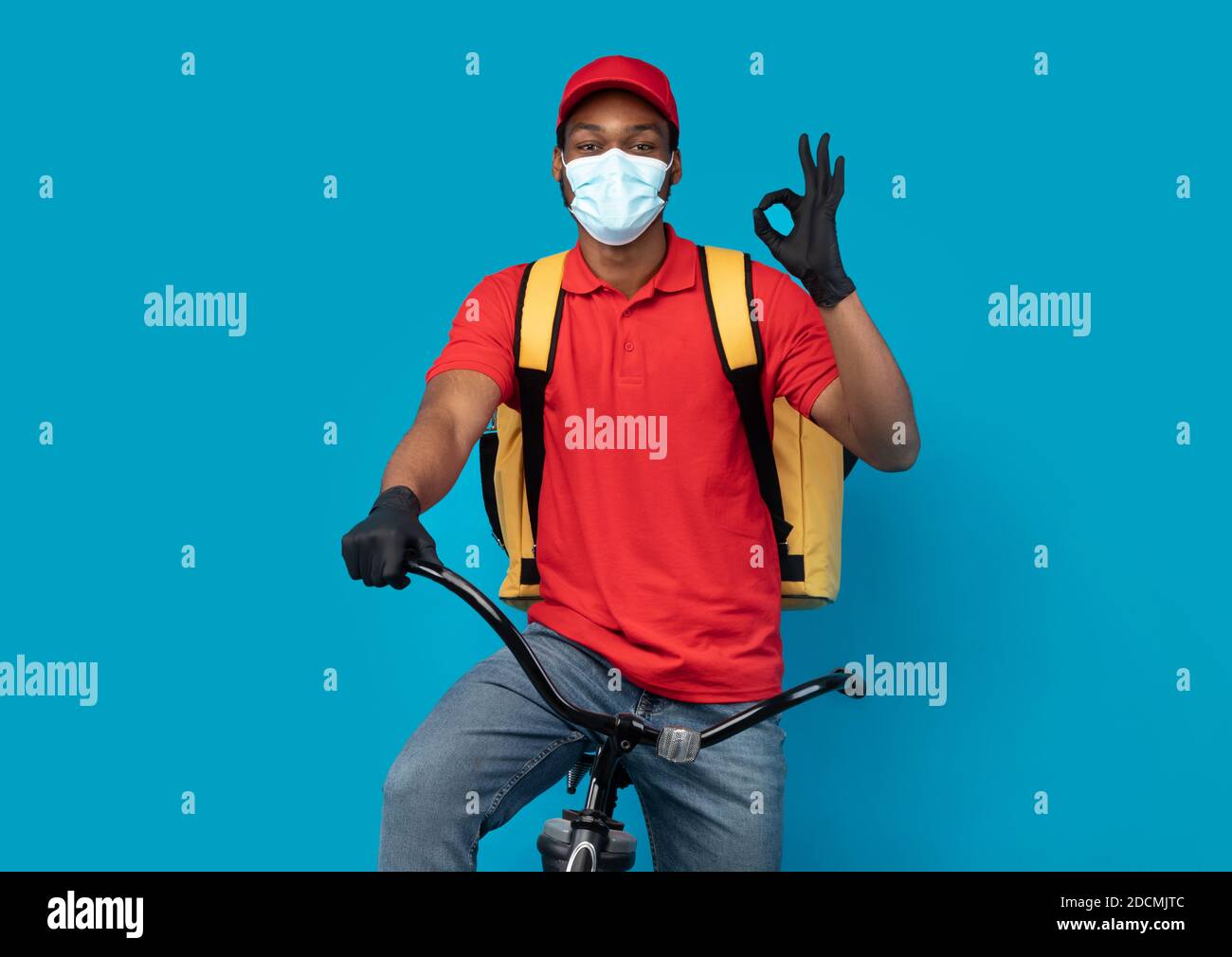 Black delivery man in mask showing okay gesture, riding bike Stock ...