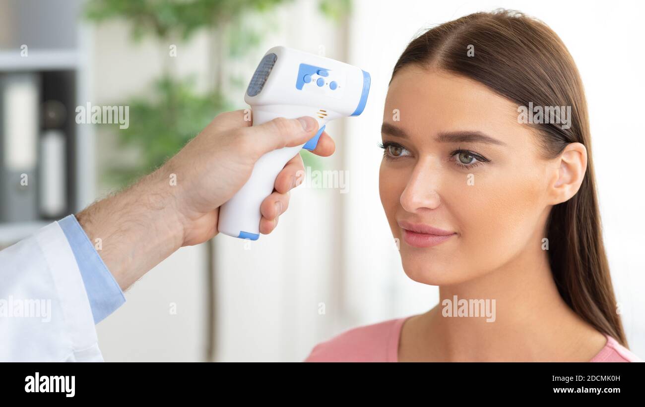 Doctor checking temperature of female patient using infrared ...