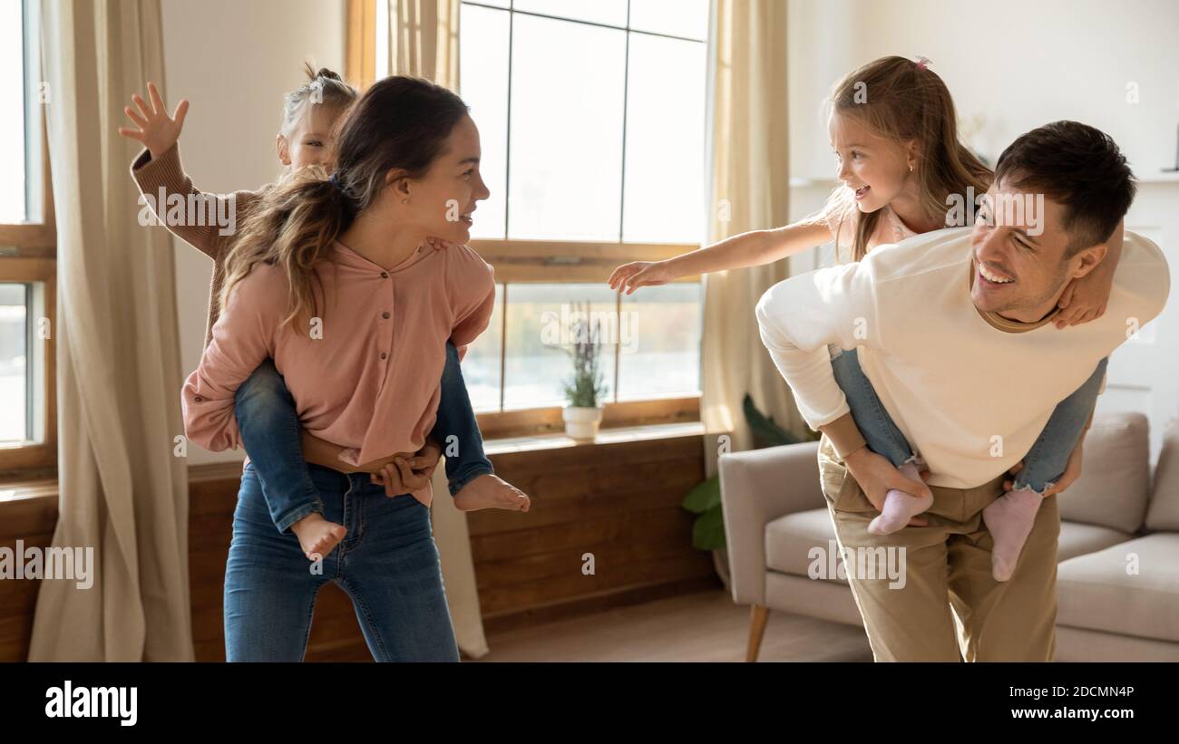 Parents piggyback riding little daughters enjoy playtime on weekend ...