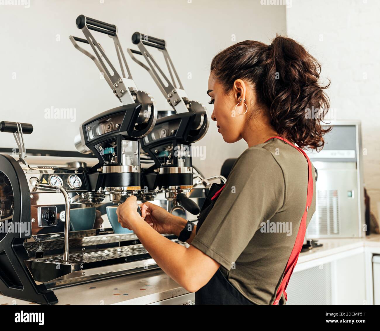Female barista using a coffee machine to make an espresso. Young cafe ...
