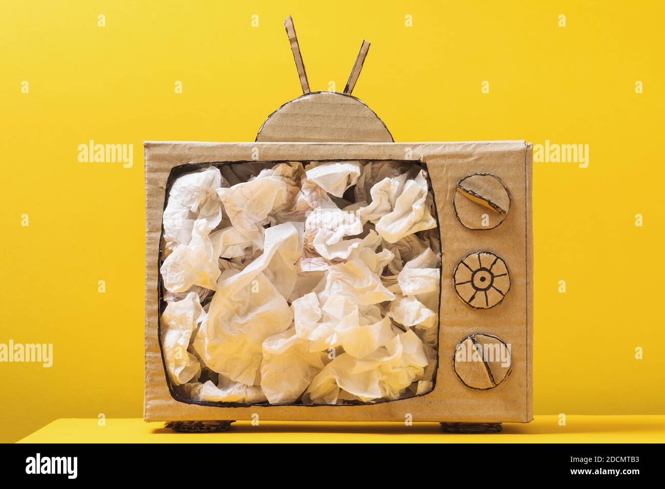Cardboard TV with rubbish in the screen on a yellow background. Concept ...