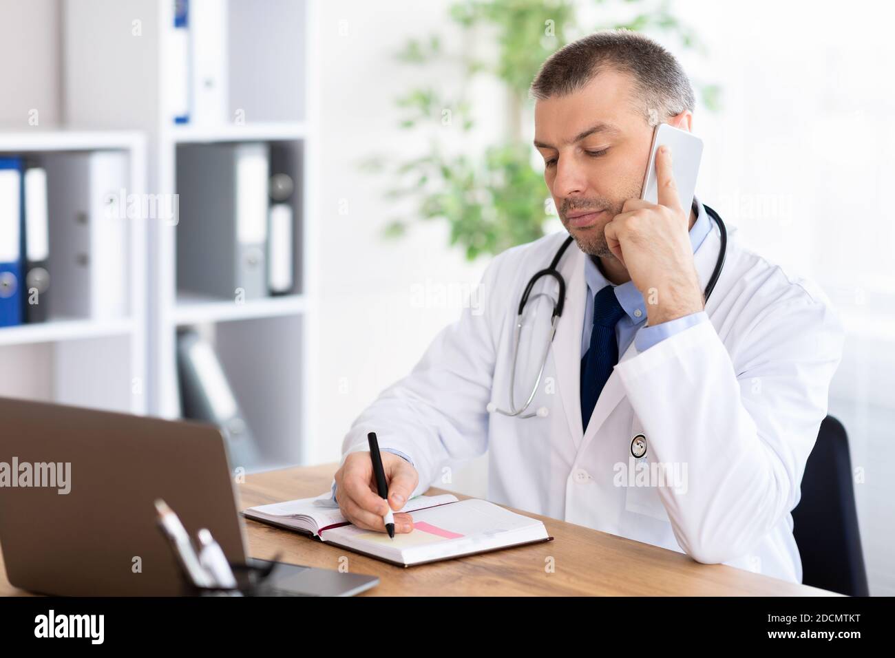 Doctor talking on smart phone with patient and writing notes Stock ...