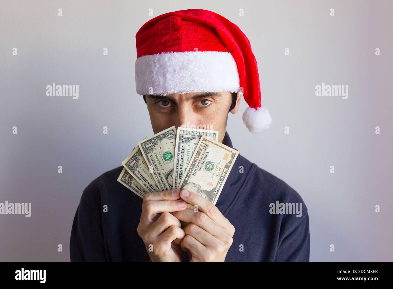 Greedy man with Santa hat holding dollar bills covering face over white ...