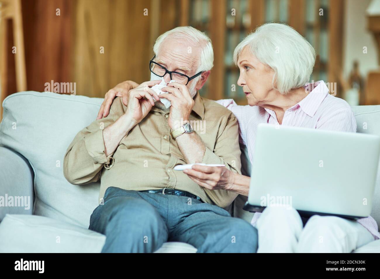 Senior wife taking care of her spouse while having online consultation ...