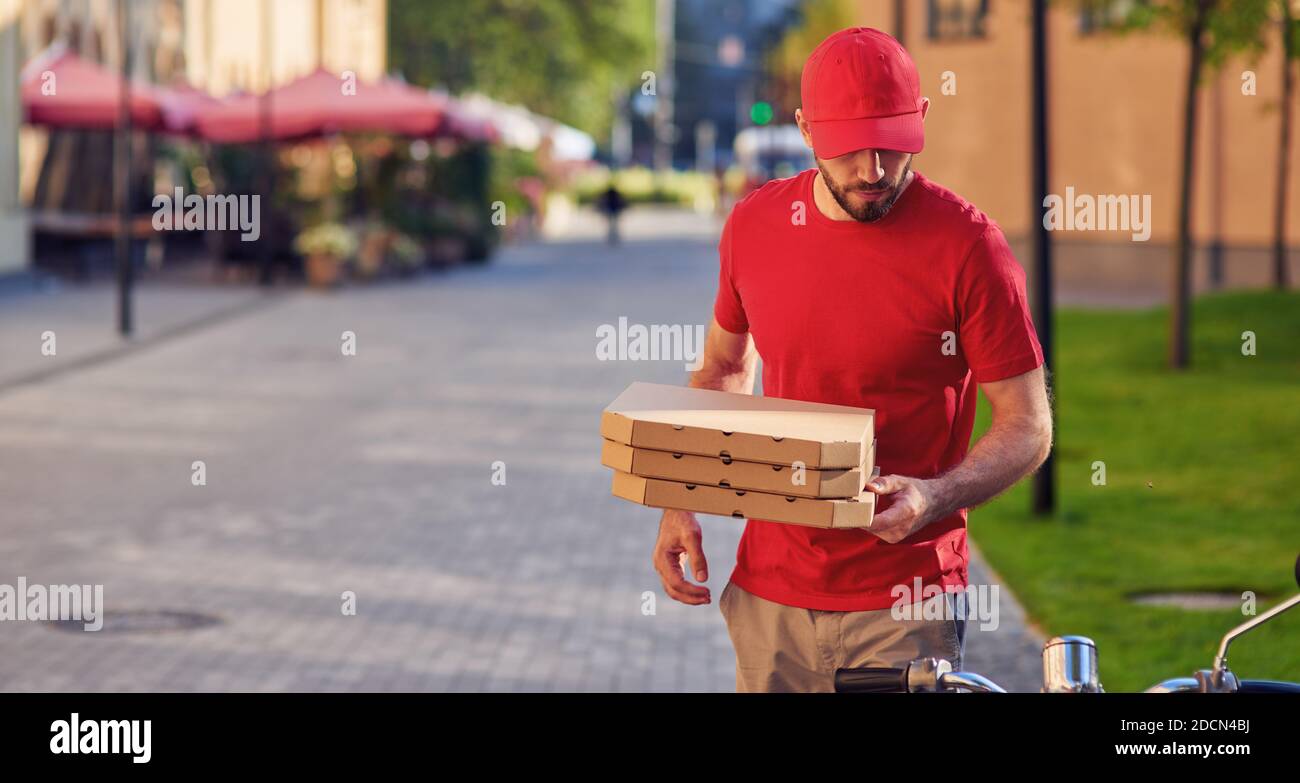 Young caucasian delivery man in red uniform delivering pizza, standing ...