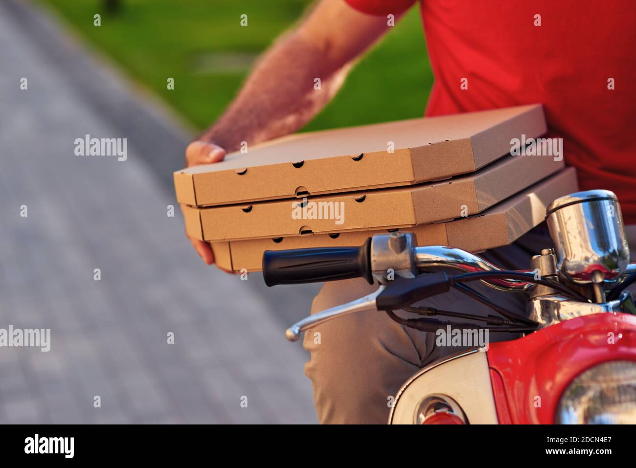 Courier in red uniform sitting on scooter and holding pizza boxes ...