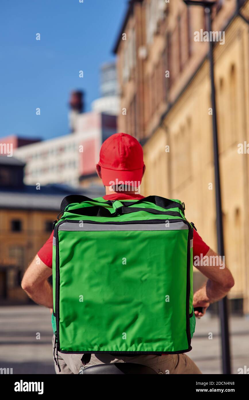 Rear view of delivery man with thermo bag riding bicycle along the ...