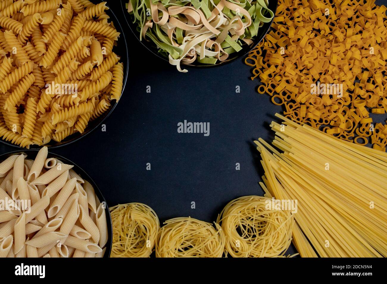 Different types of dry pasta on the plate and in bowls on black ...