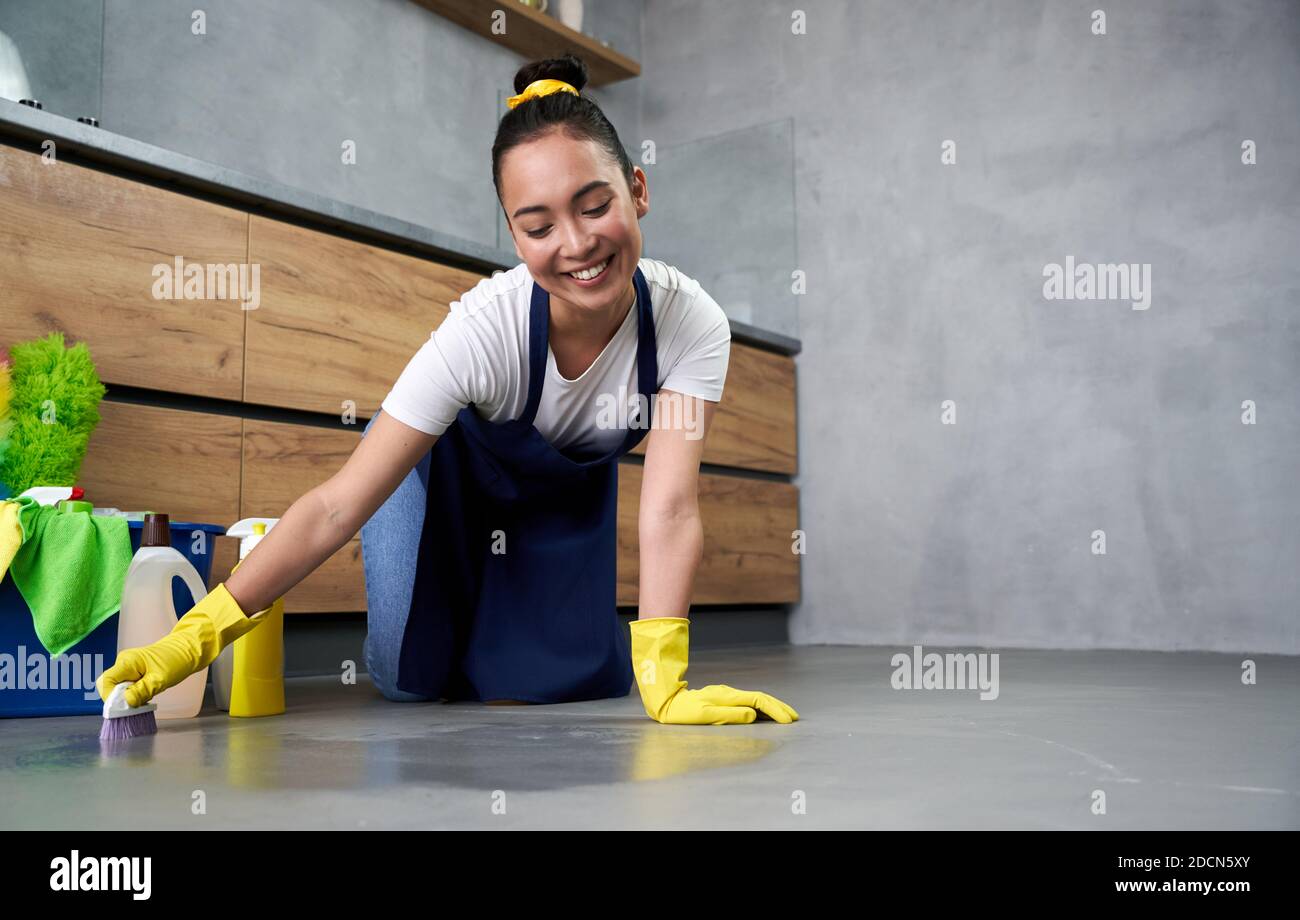Clean it all. Joyful young woman smiling while cleaning floor with ...