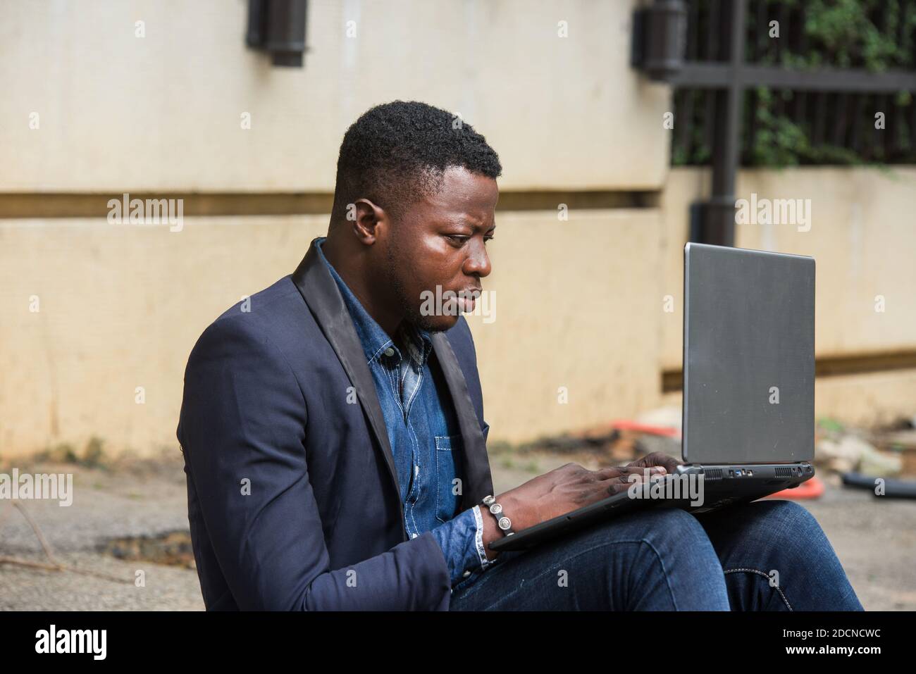 Businessman sitting outside modern office block and working on laptop ...