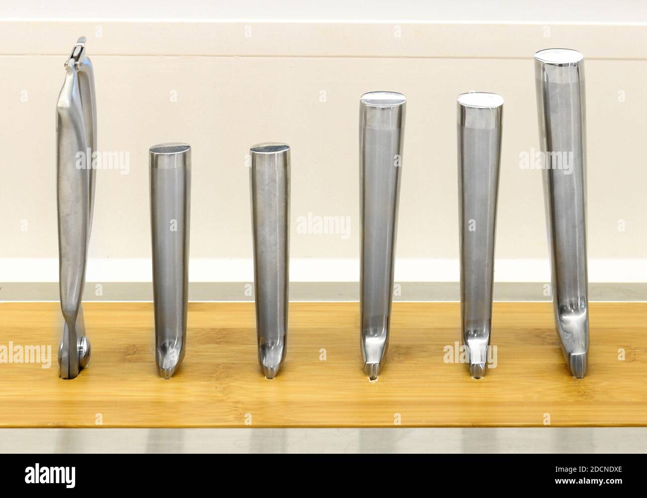 Metallic knives handles line up in wooden storage block. Flat view ...